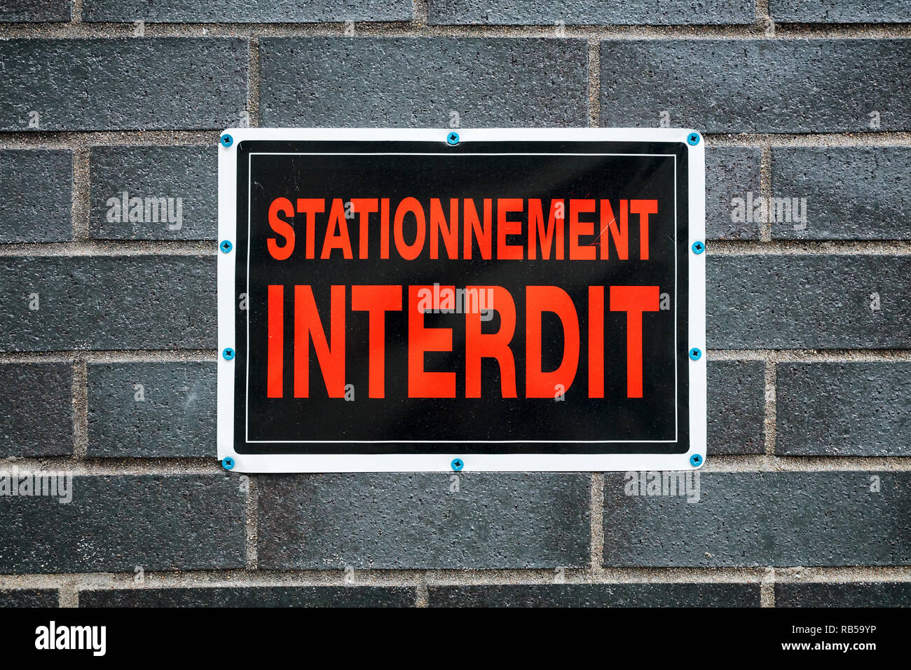 No parking sign in French mounted on a gray brick wall. Stationnement ...