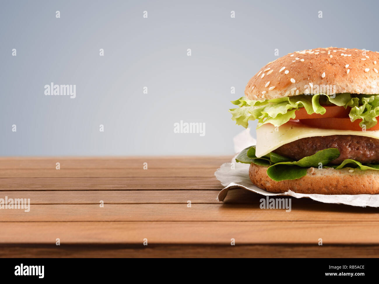 Classic beef burger with cheese, tomatoes and salad on wooden table ...