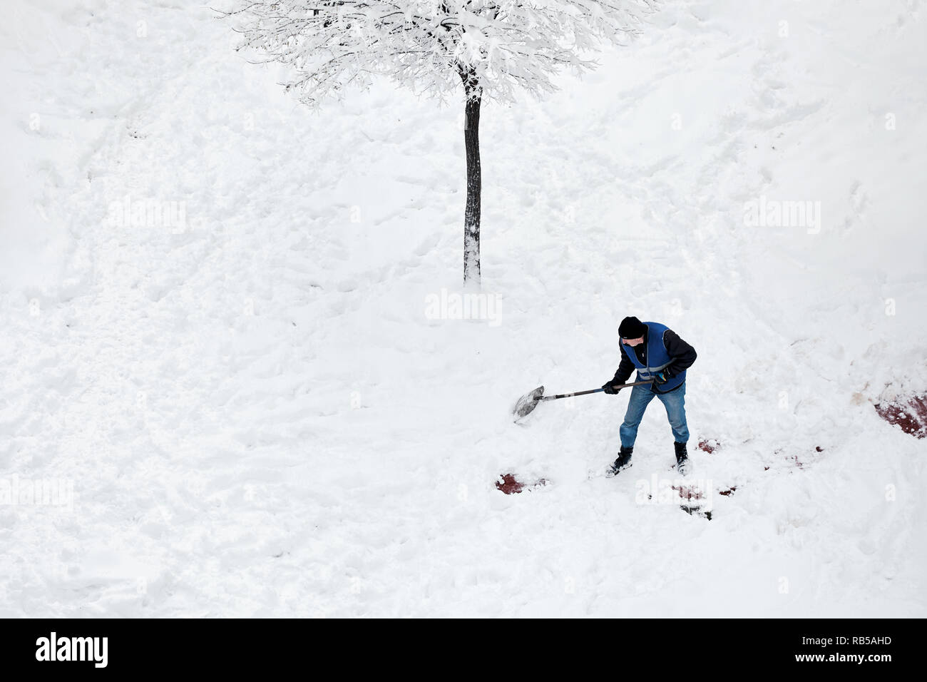 Male worker in uniform shoveling snow in the yard after a snowstorm in ...
