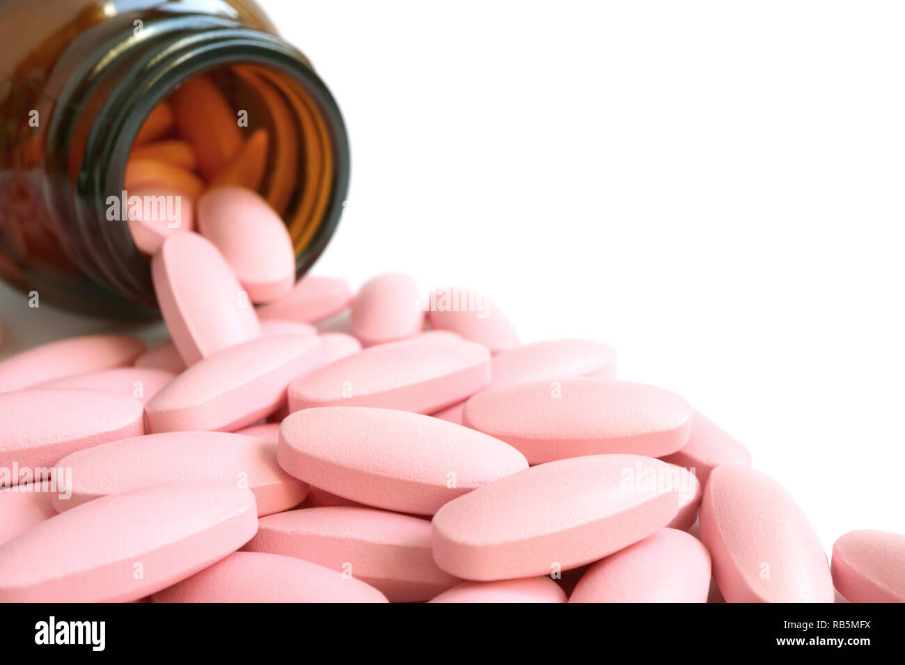 Heap of pastel pink oval shaped pills scattered from smoky brown glass ...