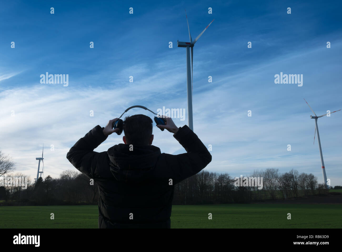 Man infront of a wind farm uses noise protector to reduce the noise of ...