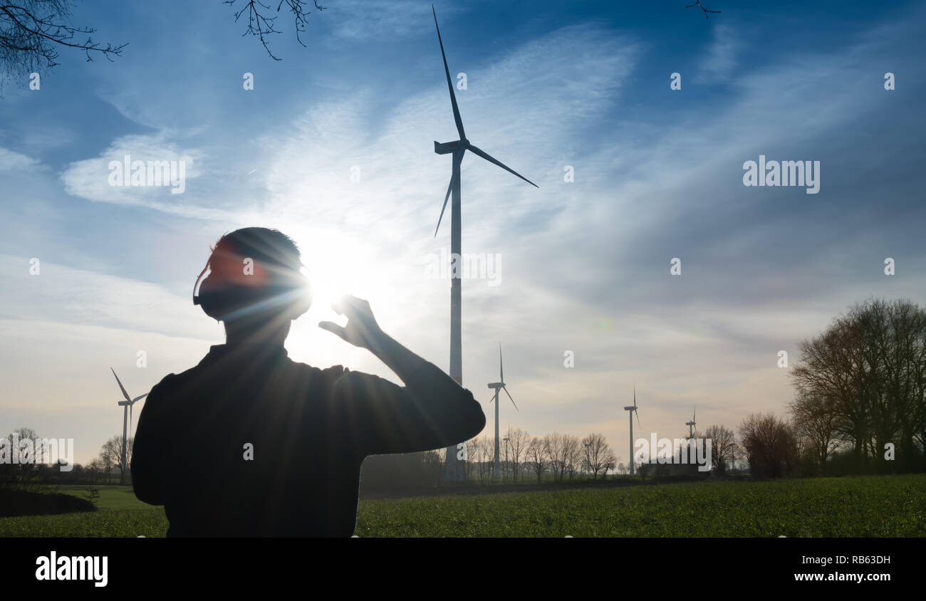 Man infront of a wind farm uses noise protector to reduce the noise of ...