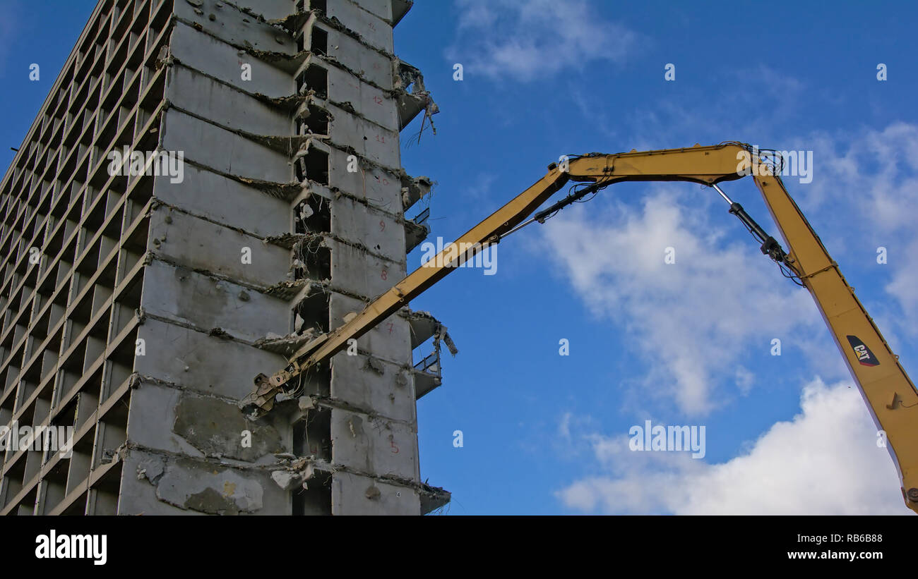 Yellow construction crane arm demolishing a stripped down concrete ...