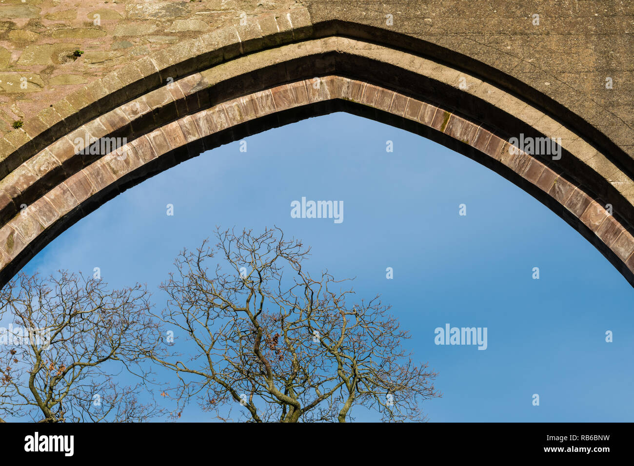 Ancient stone arch in medieval ruins of an old church frames a blue sky ...