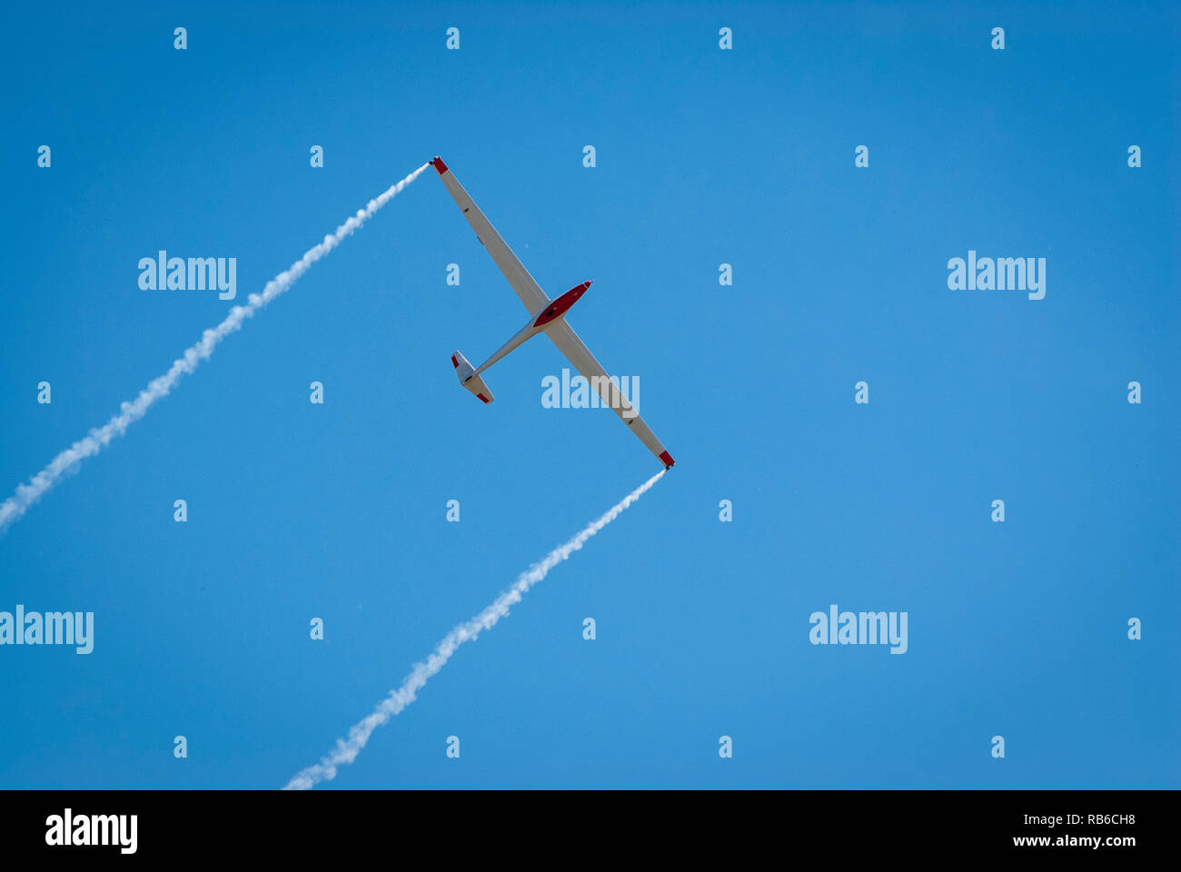 A acrobatic glider trailing smoke trails from its wings against a ...