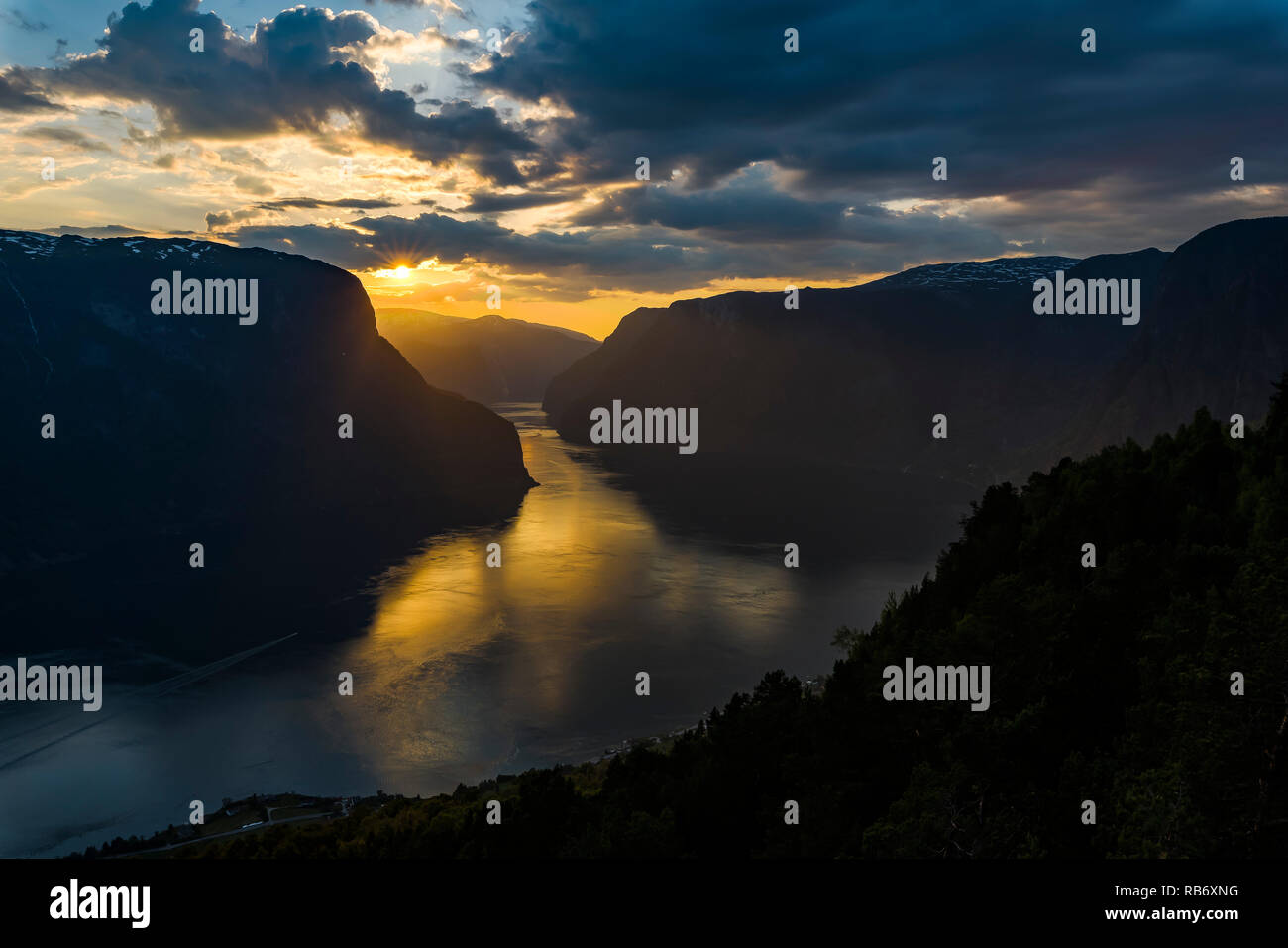A golden sunset over rocky walls falling into the fjord waters, under a ...