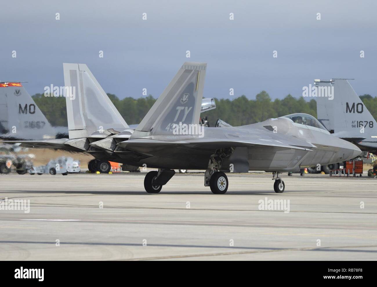 A U.S. Air Force F-22 Raptor taxies past a line of F-15E Strike Eagles ...