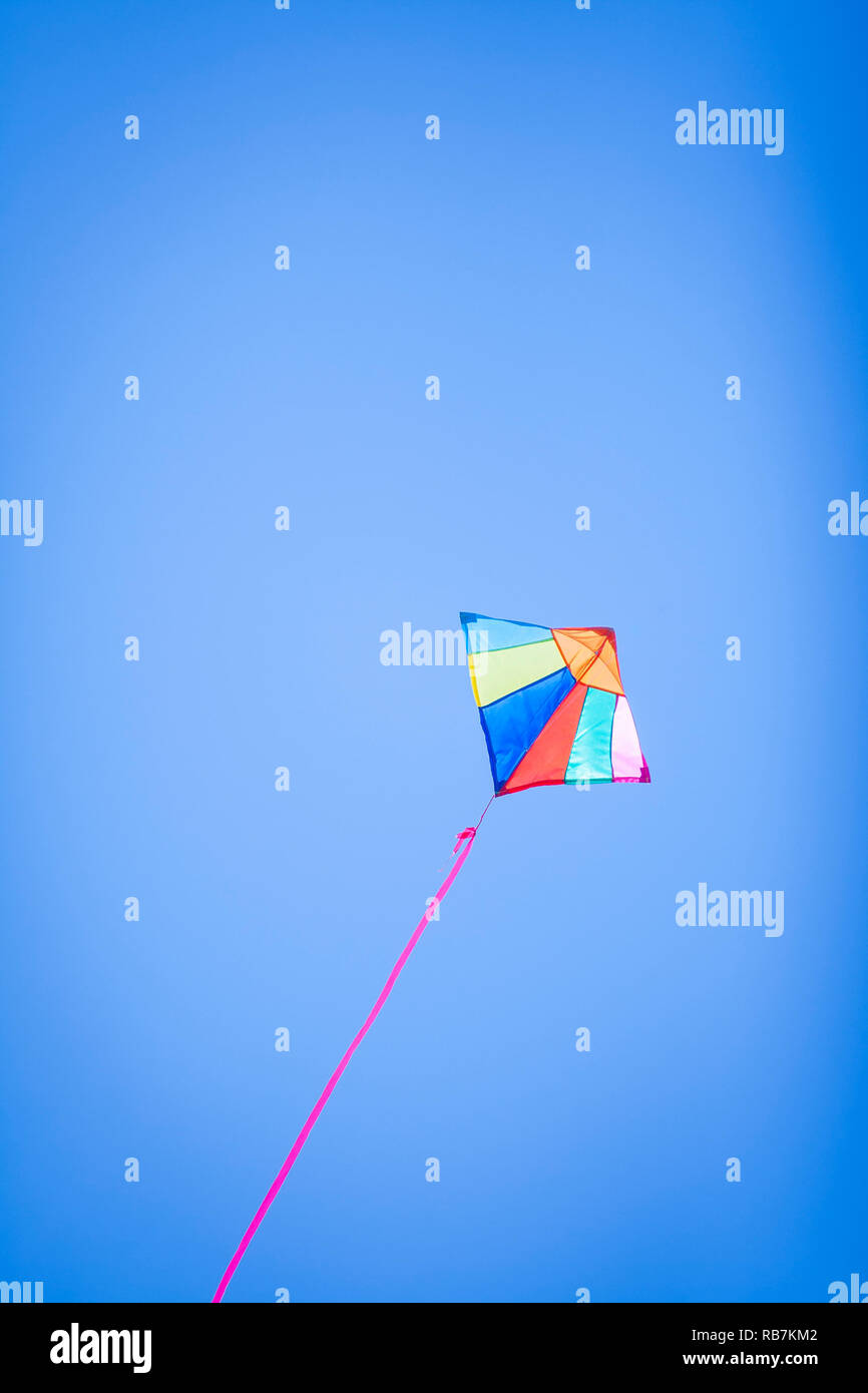 Colorful, traditional, diamond shaped kite soaring with a blue sky ...