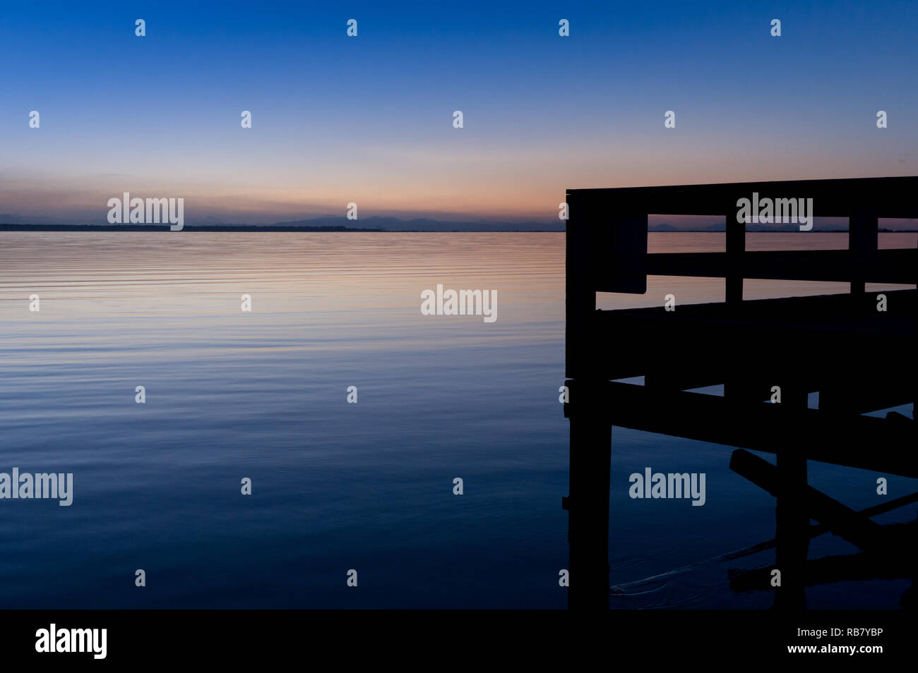 Silhouette of pier overlooking calm ocean water at entrance to Mud Bay ...