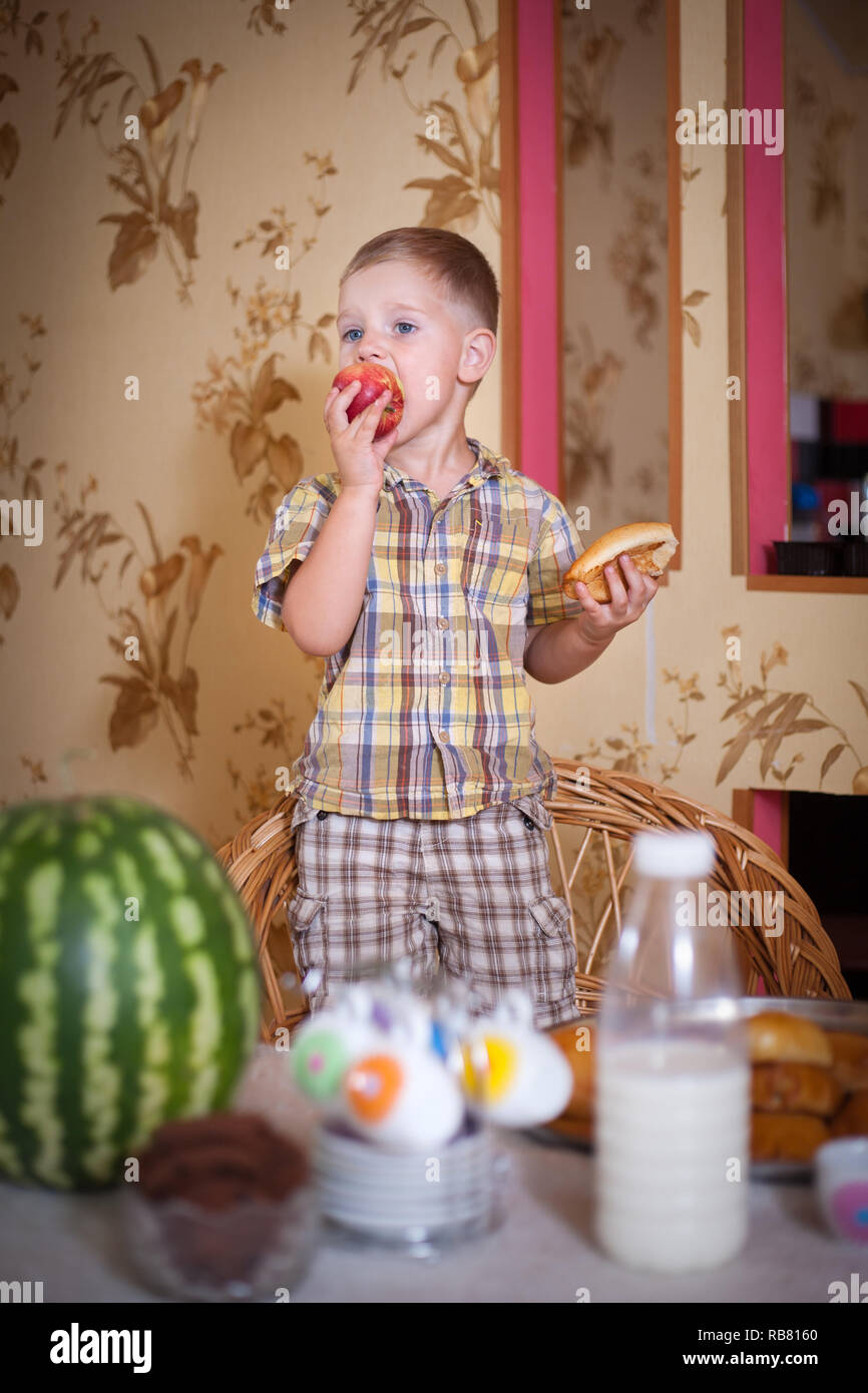 Little boy eating a pie in the kitchen at the table. Shooting in the ...