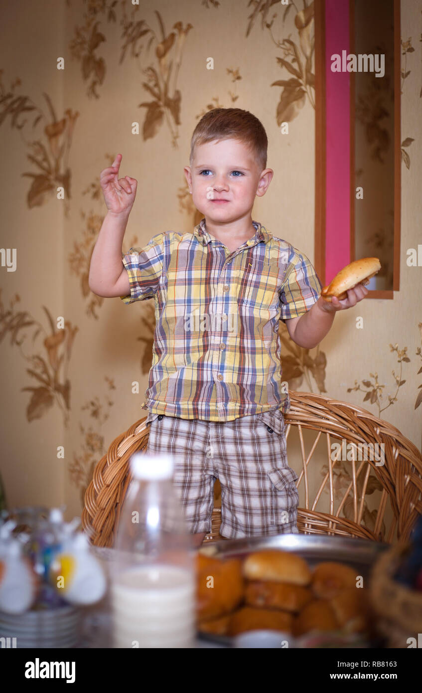 Little boy eating a pie in the kitchen at the table. Shooting in the ...