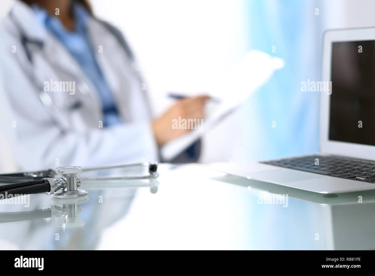Stethoscope lying on glass desk with laptop computer at busy physician ...
