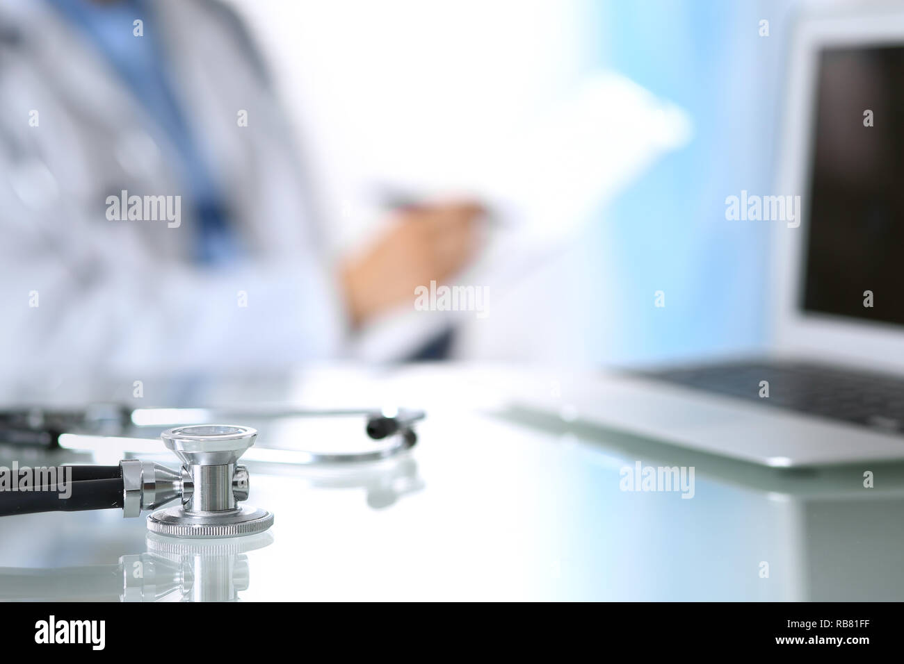 Stethoscope lying on glass desk with laptop computer at busy physician ...