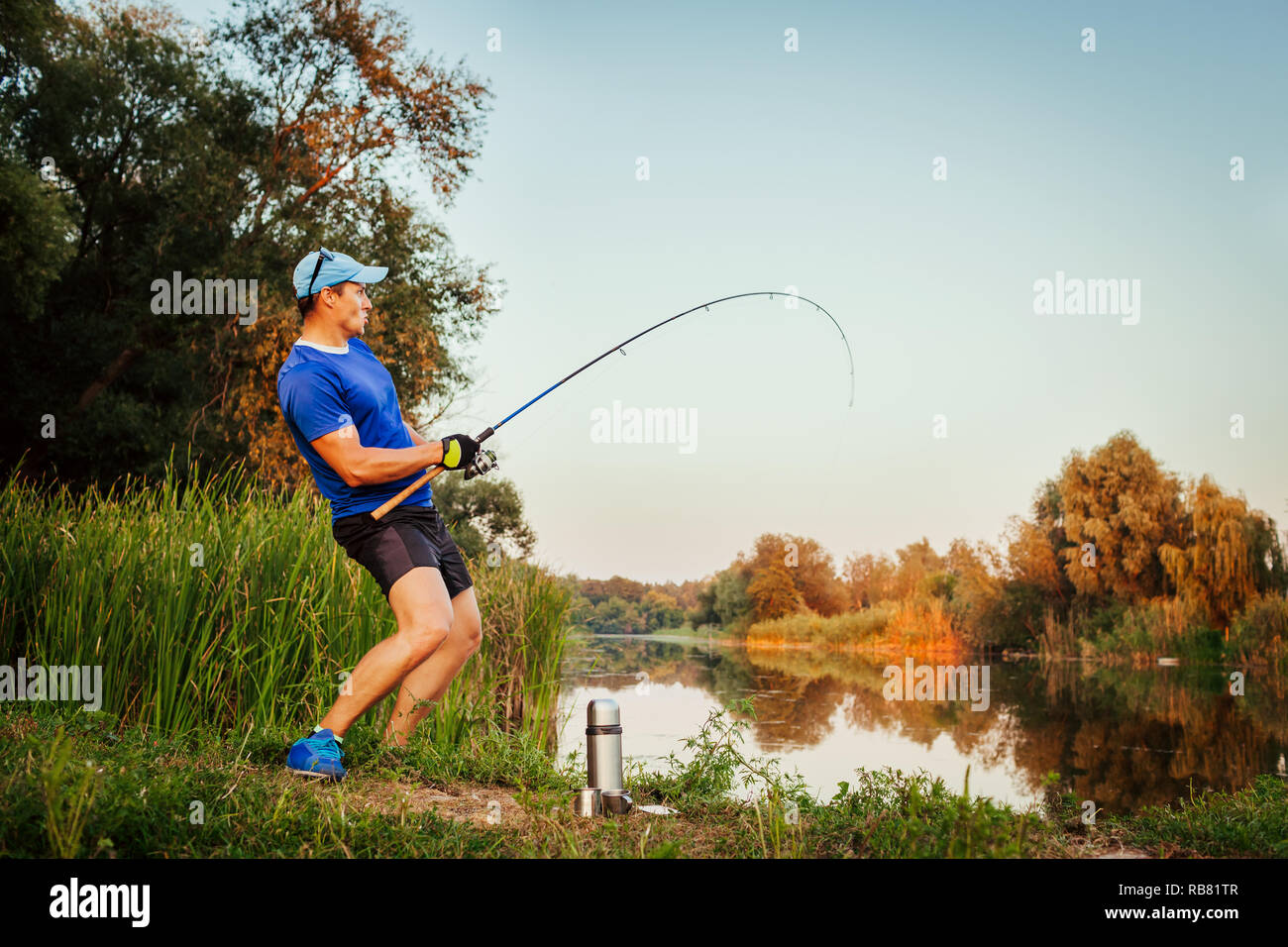 Young man fishing on river at sunset. Happy excited fiserman pulling ...