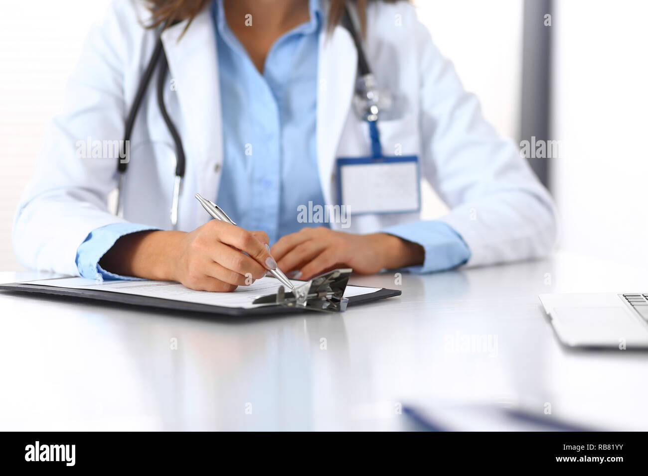 Unknown doctor woman filling up medical form while sitting at the desk ...