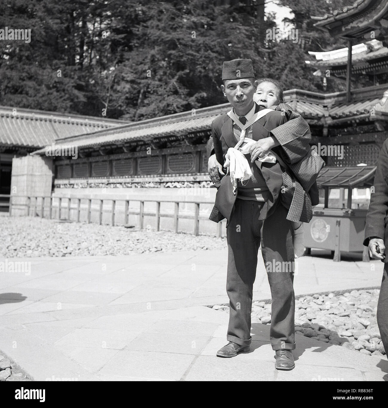 1950s, historical, visiting a temple, a Japanese man carrying an adult ...
