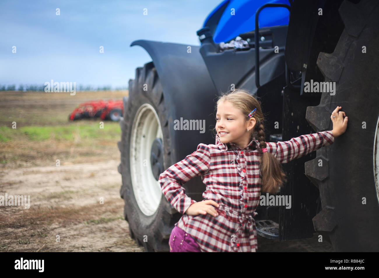 Cute girl near the modern tractor in the field. The concept of field ...