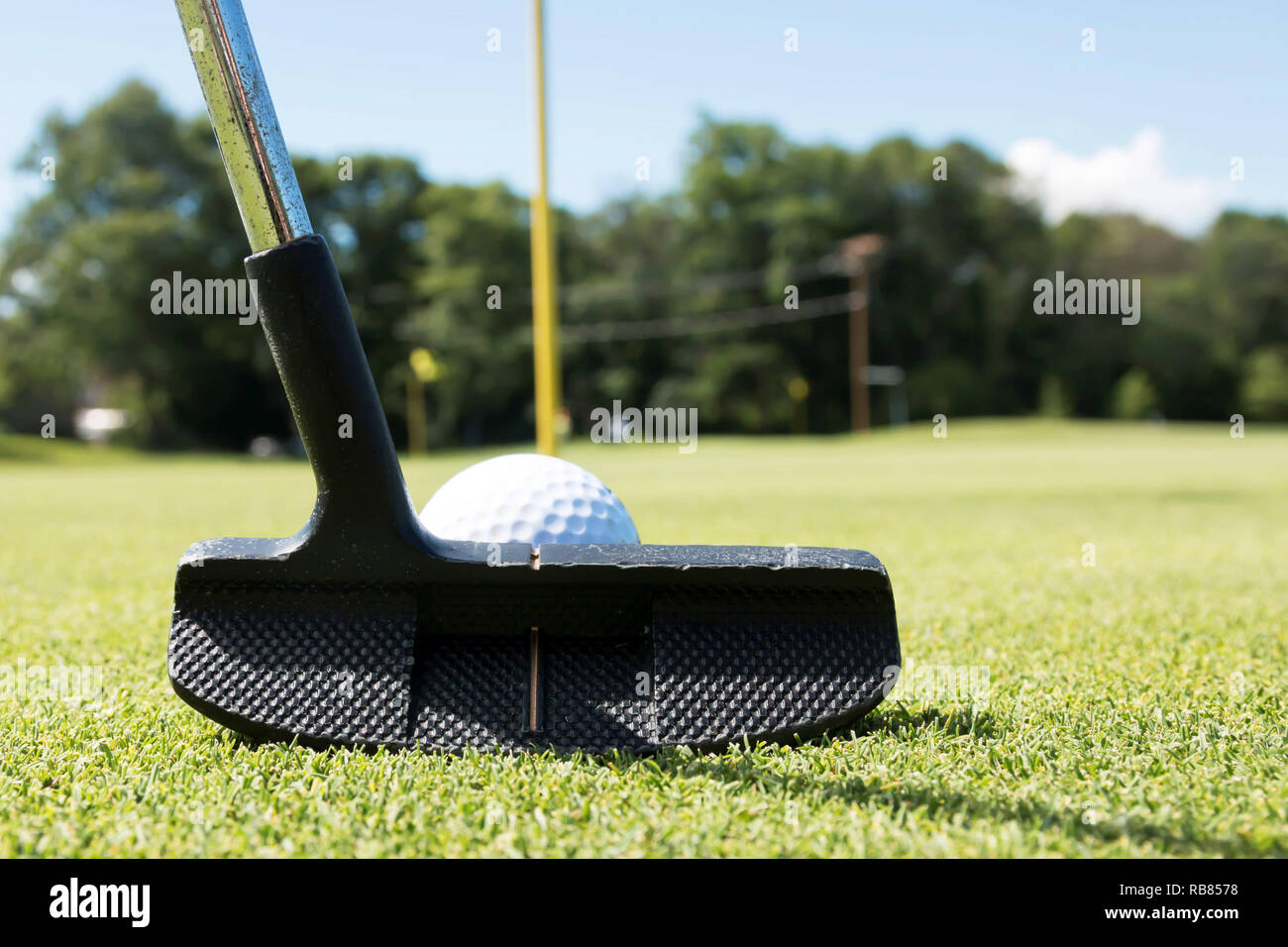 A putter is lined up behind a white golf ball with the yellow pin on ...
