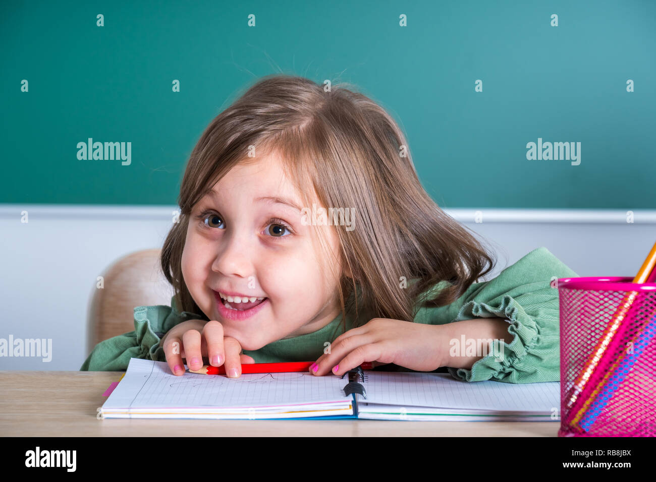 Little pretty girl sitting in the classroom at the gray desk and posing ...