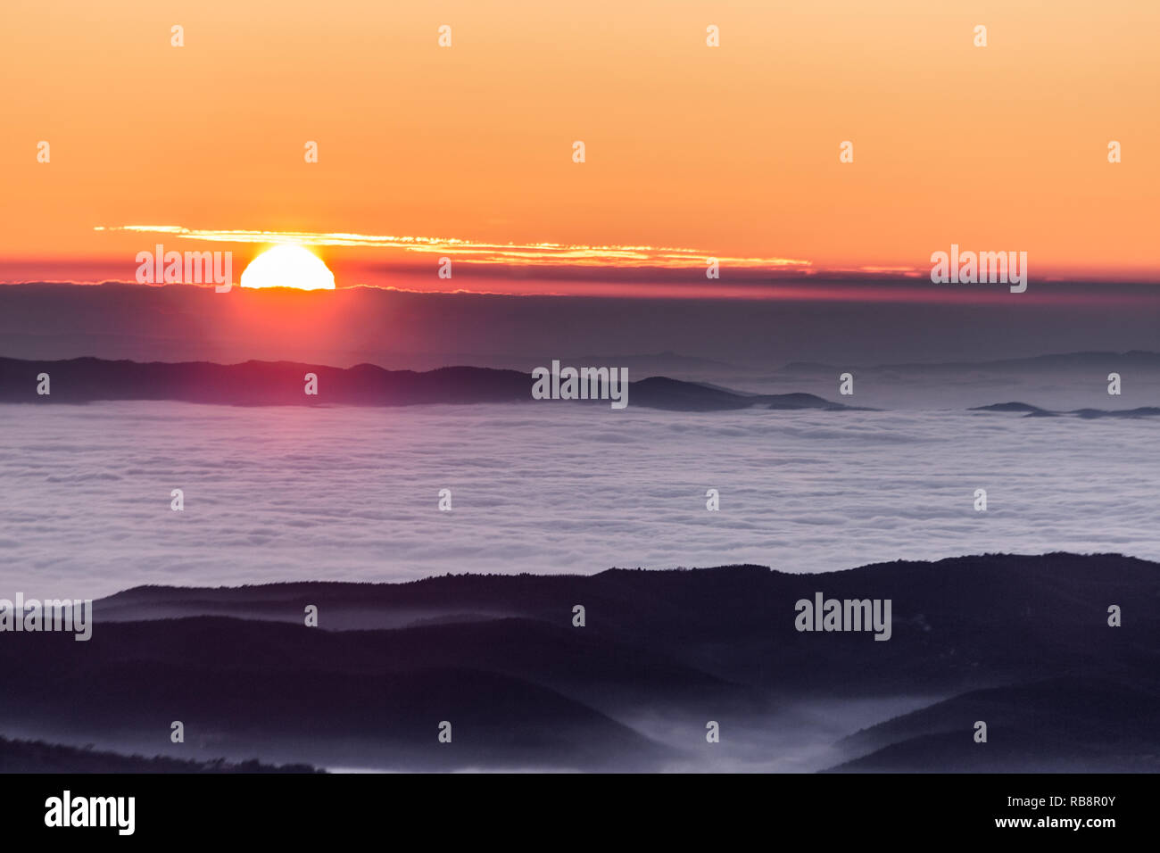 Beautiful sunset over a valley filled by fog with mountains and hills ...