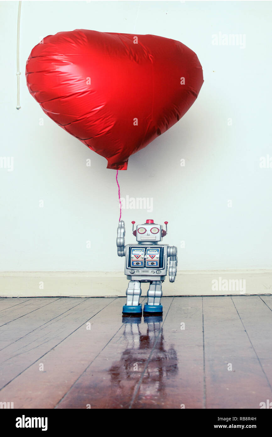 retro silver robot holding a big red balloon standing on an old wooden ...