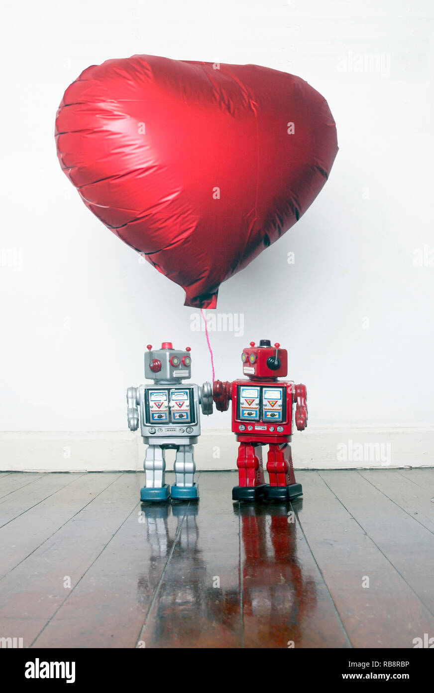 two retro tin robots together holding a red balloon standing on an old ...