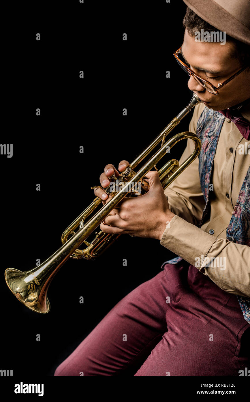 mixed race male jazzman in hat and eyeglasses playing on trumpet ...