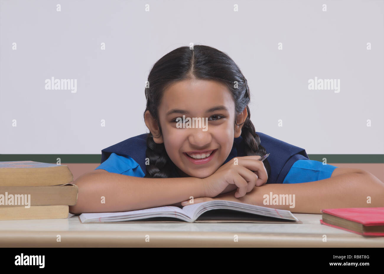 Portrait of school girl leaning on table while studying in classroom ...