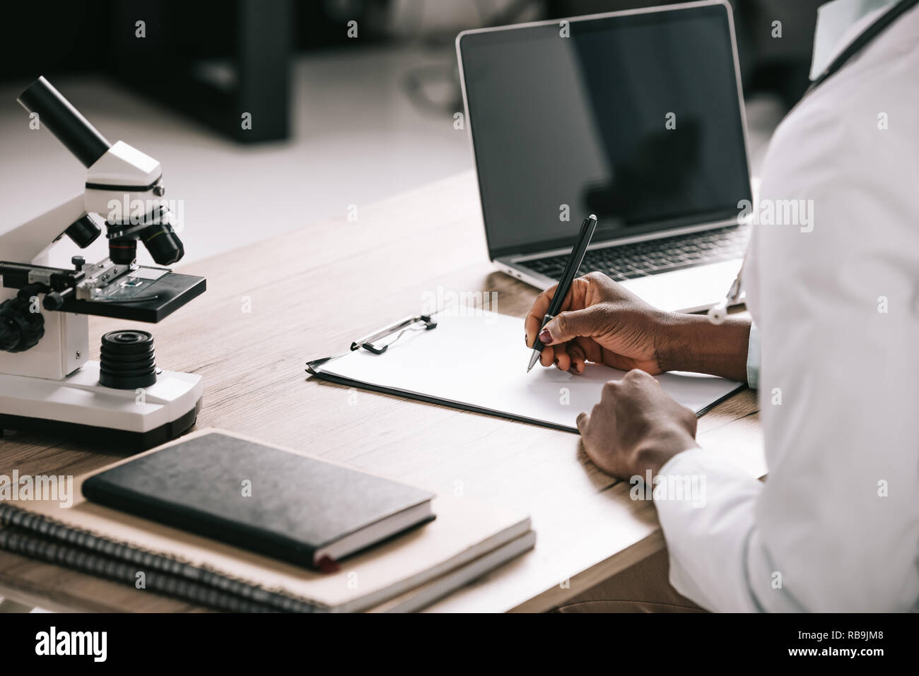 cropped view of african american scientist writing on paper near laptop ...