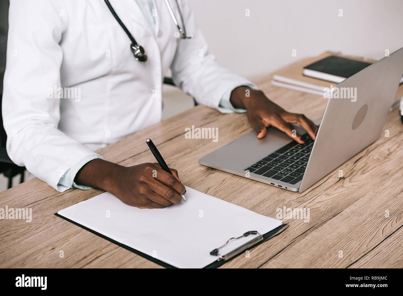 cropped view of african american scientist writing on paper and typing ...