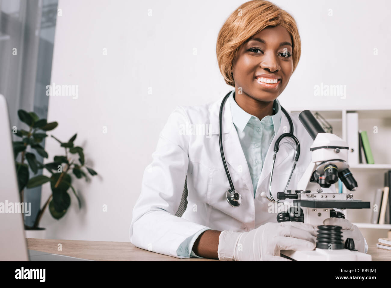 cheerful female african american scientist holding microscope in ...