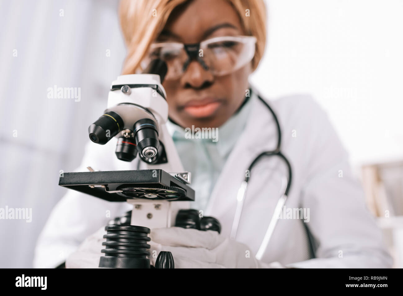 selective focus of microscope with female african american scientist on ...
