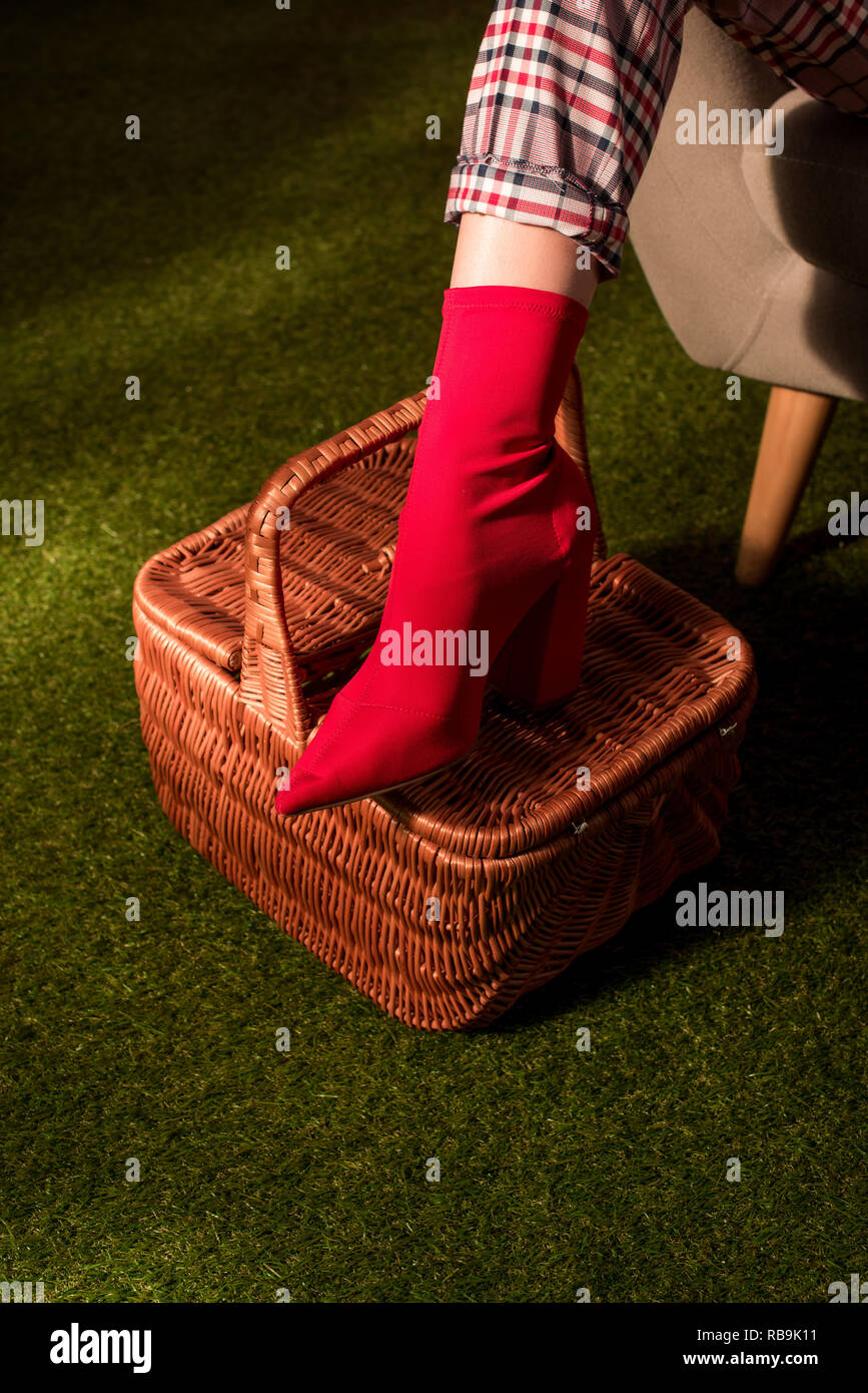 partial view of fashionable woman in red shoe posing with basket on ...