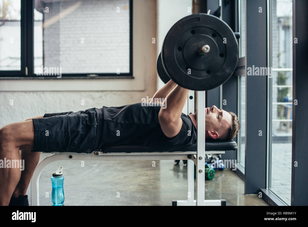 side view of handsome sportsman lifting barbell with weights while ...