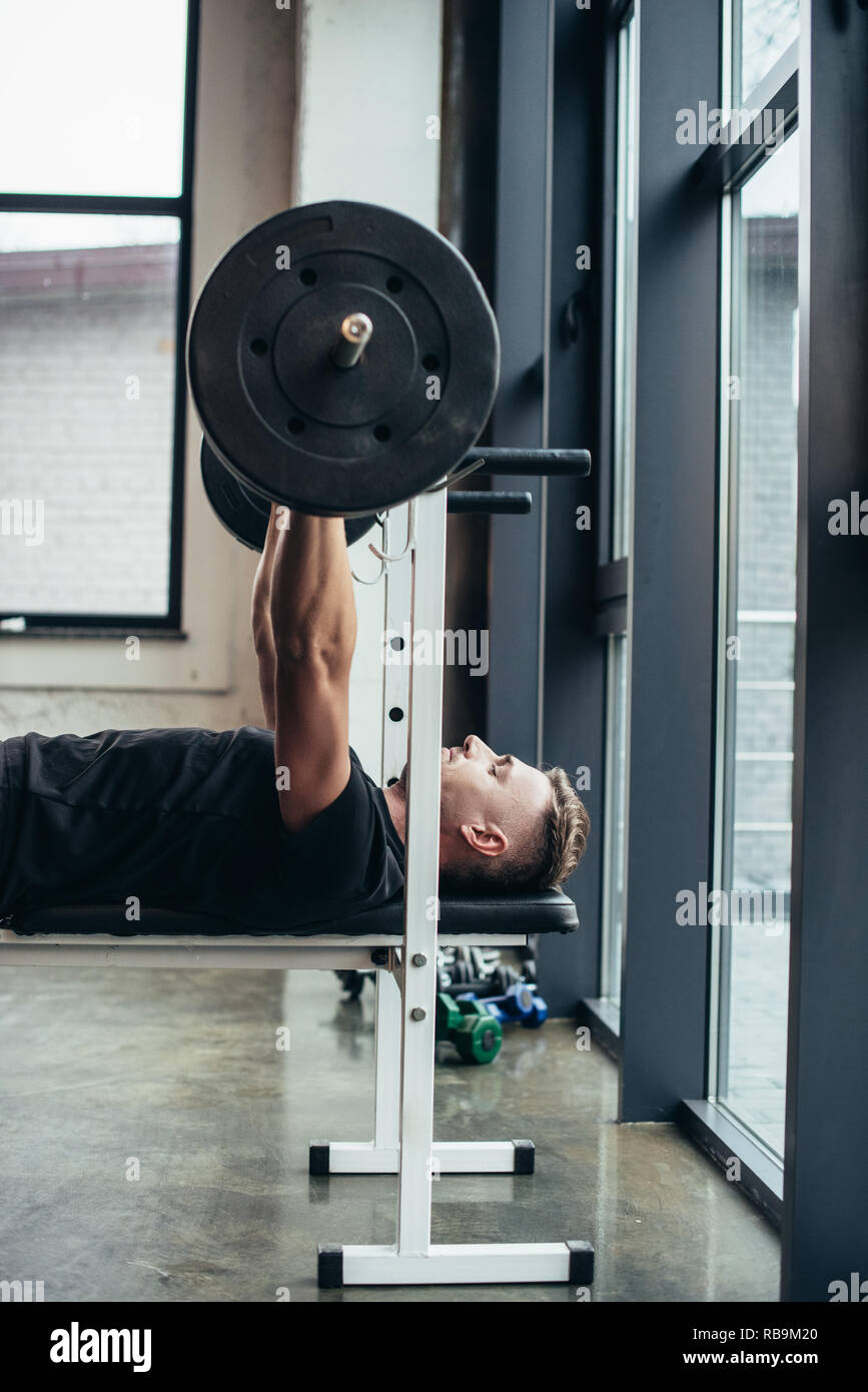 side view of handsome athletic man lifting barbell with weights while ...