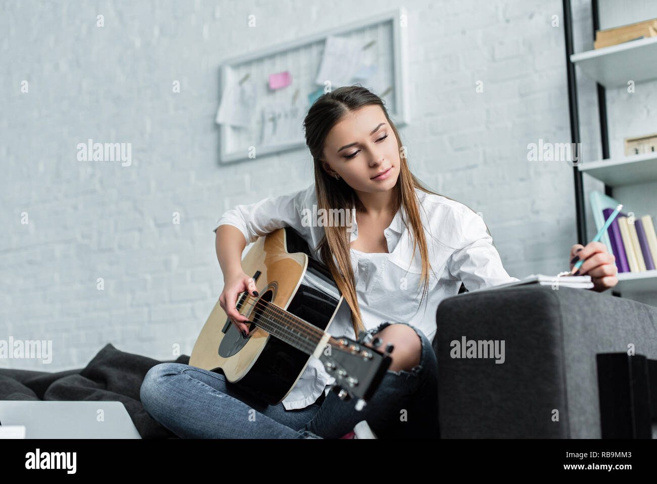 beautiful girl sitting on couch with guitar, writing in notebook and ...