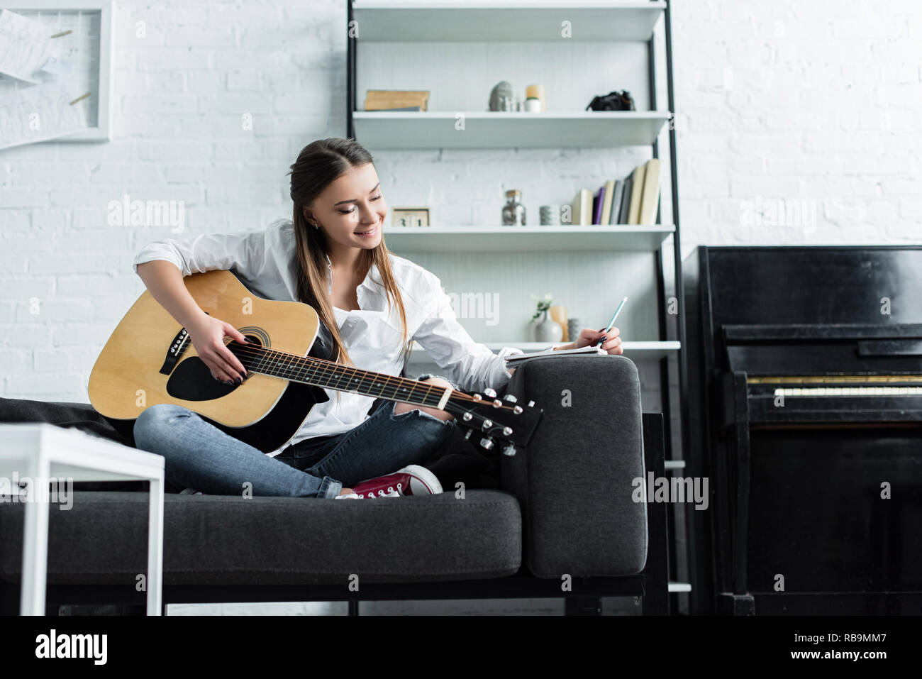 smiling girl sitting on couch with guitar, writing in notebook and ...