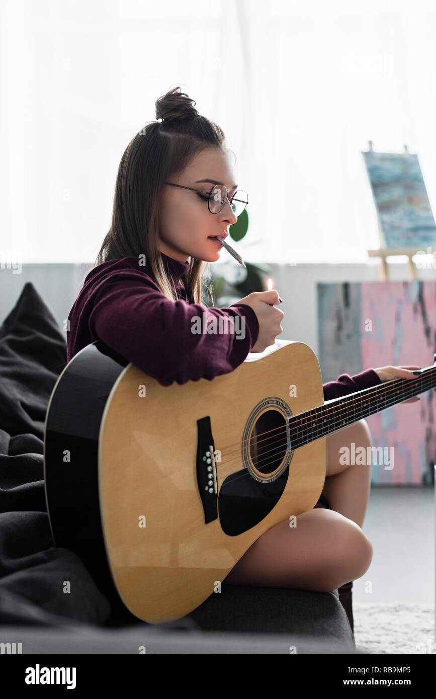 attractive girl sitting on couch, lighting marijuana joint and holding ...