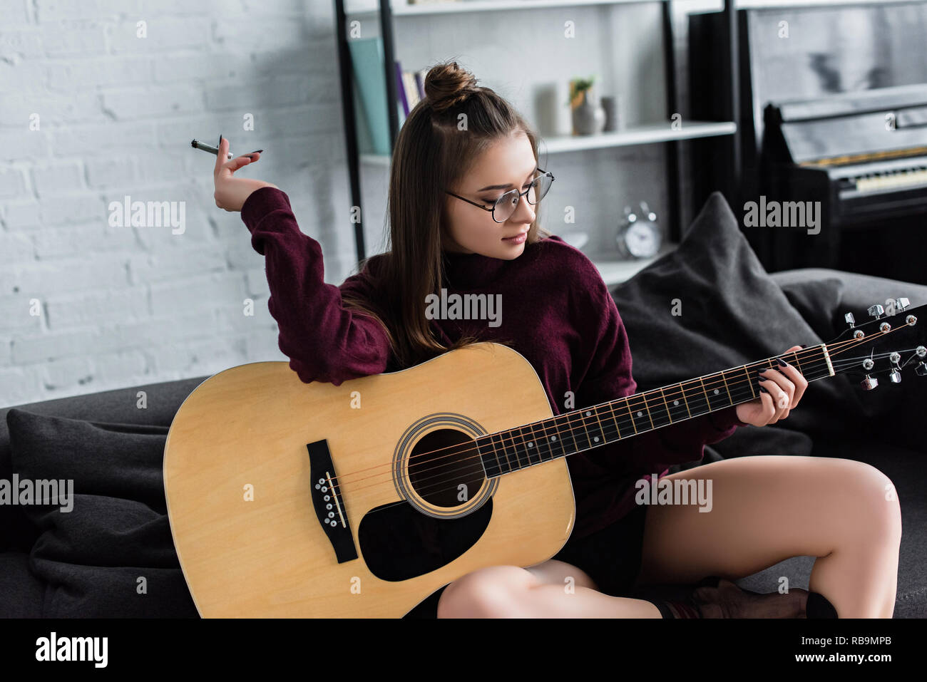 attractive girl sitting, holding marijuana joint and playing guitar at ...