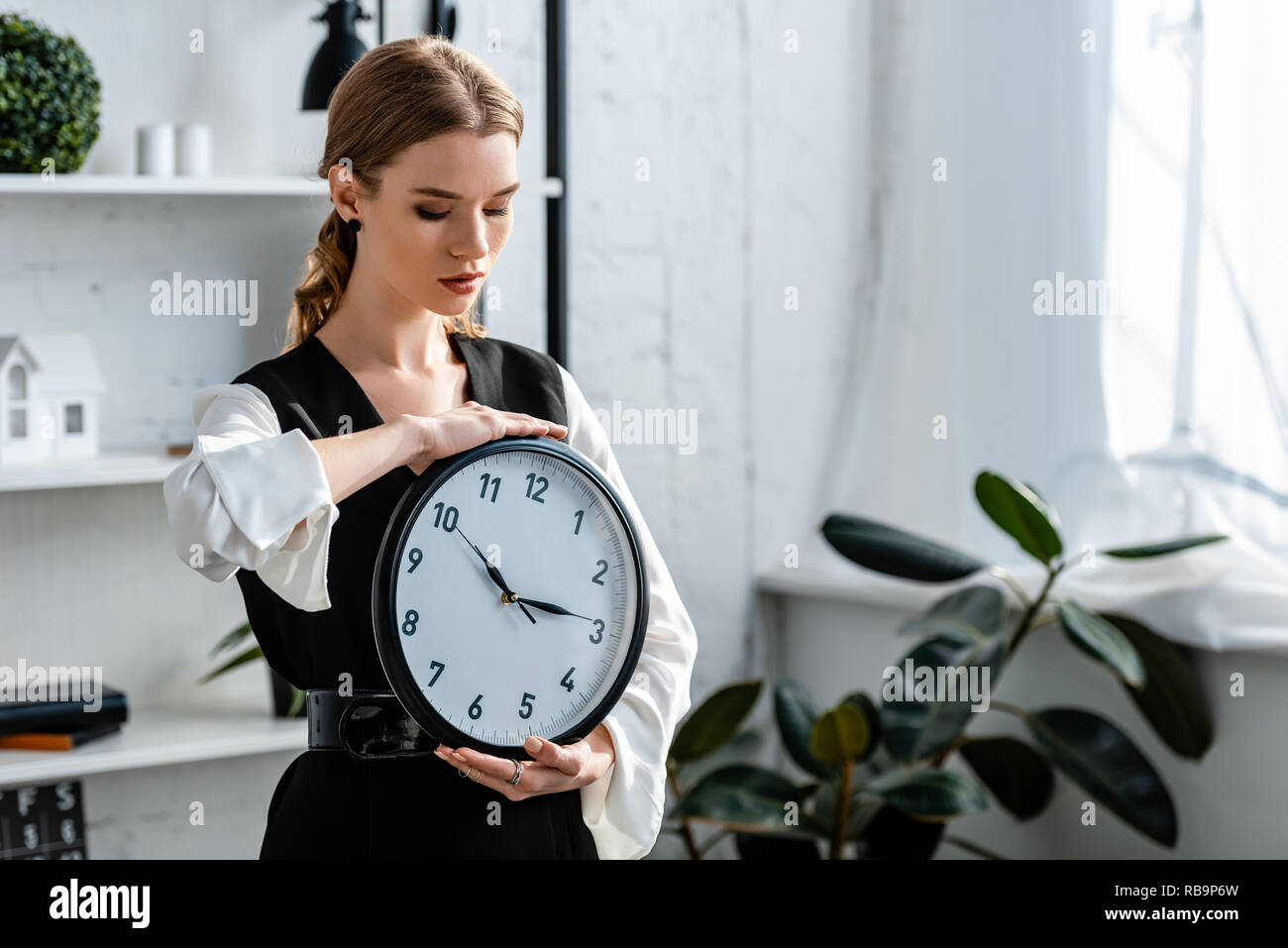attractive woman in formal wear holding clock at workplace Stock Photo ...
