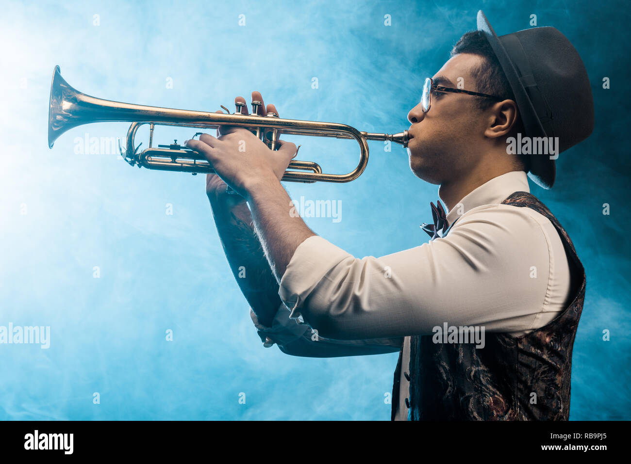 side view of jazzman playing on trumpet on stage with dramatic lighting ...