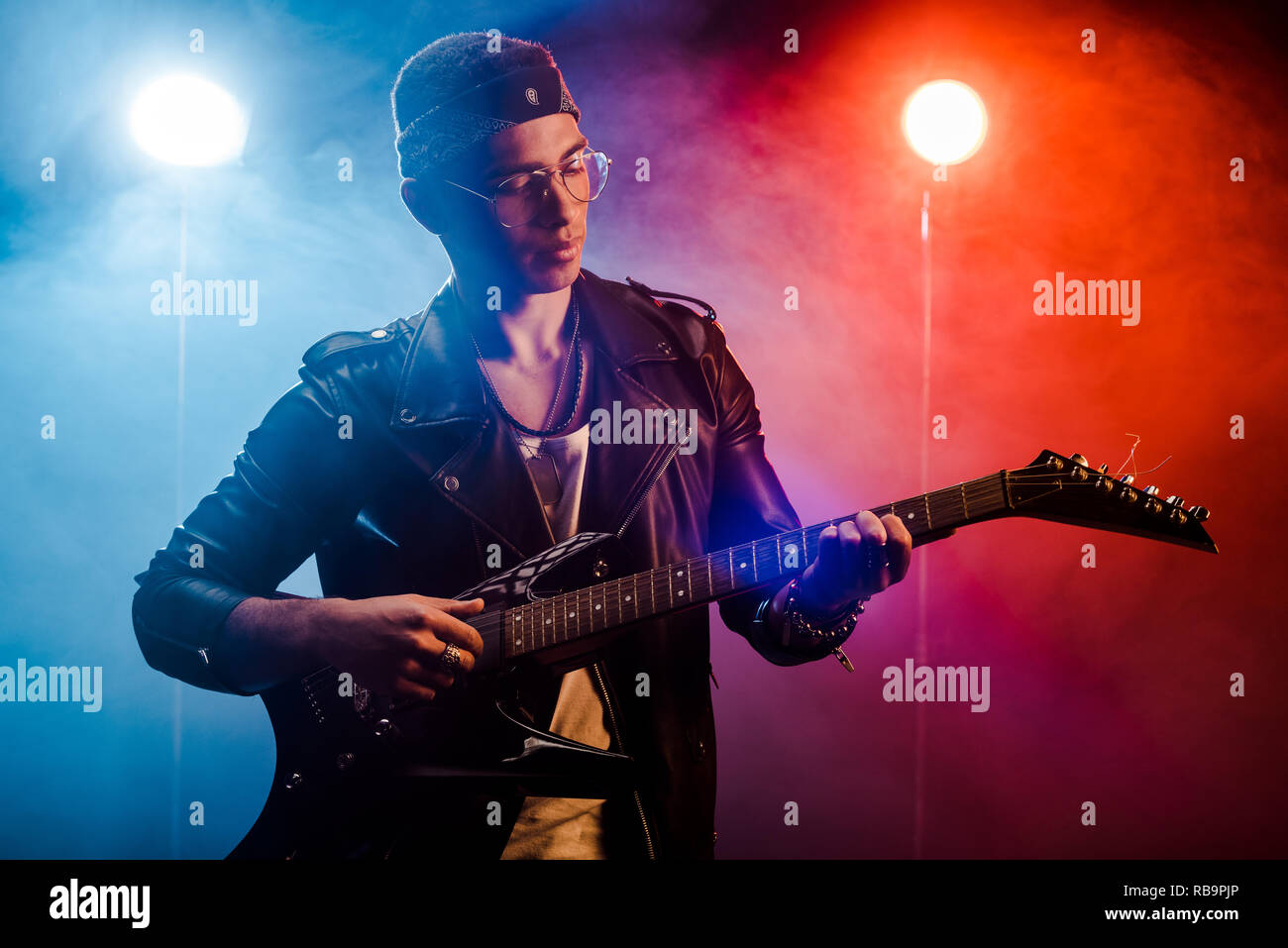 focused male musician in leather jacket performing on electric guitar ...