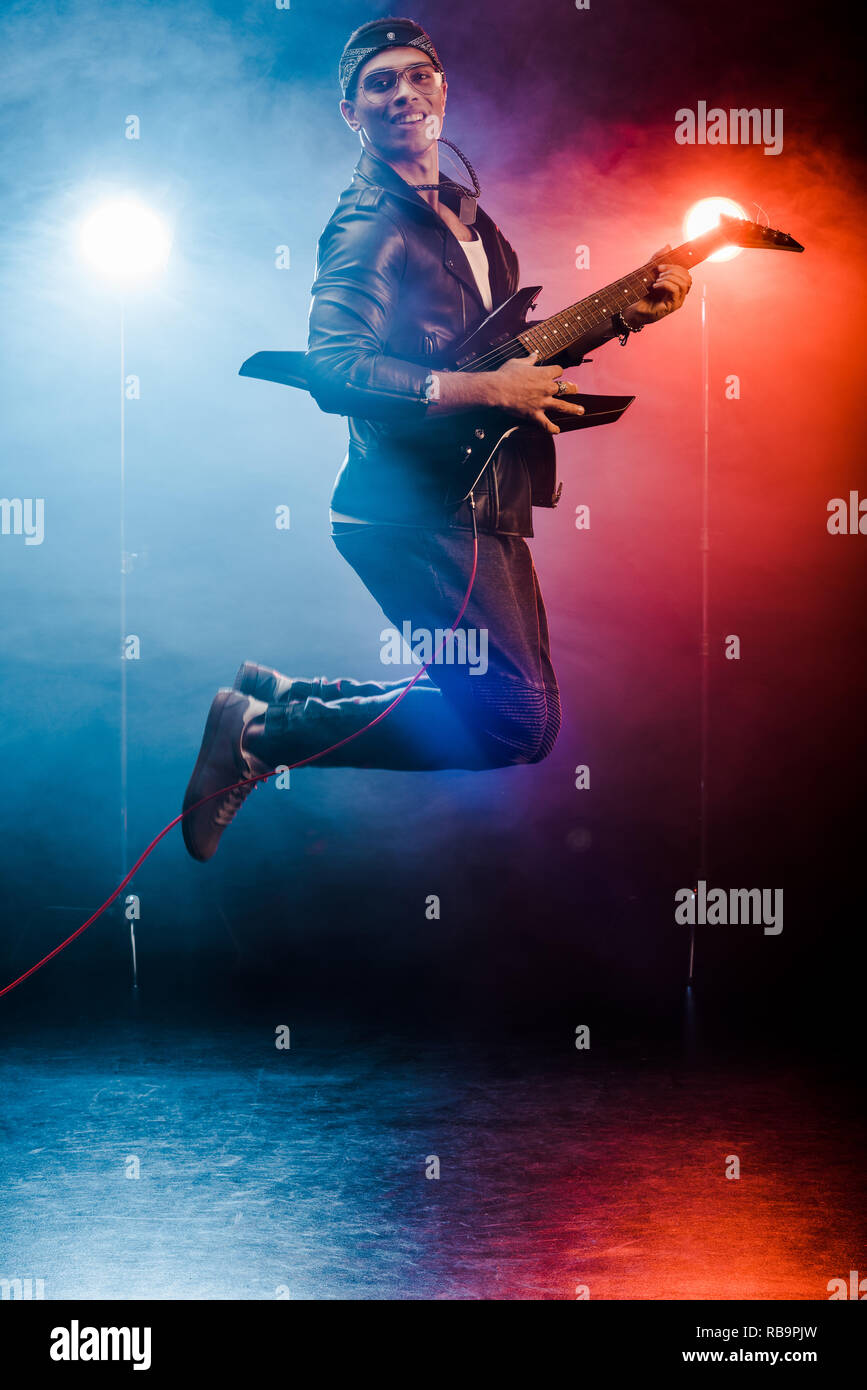 happy male musician jumping and performing on electric guitar during ...