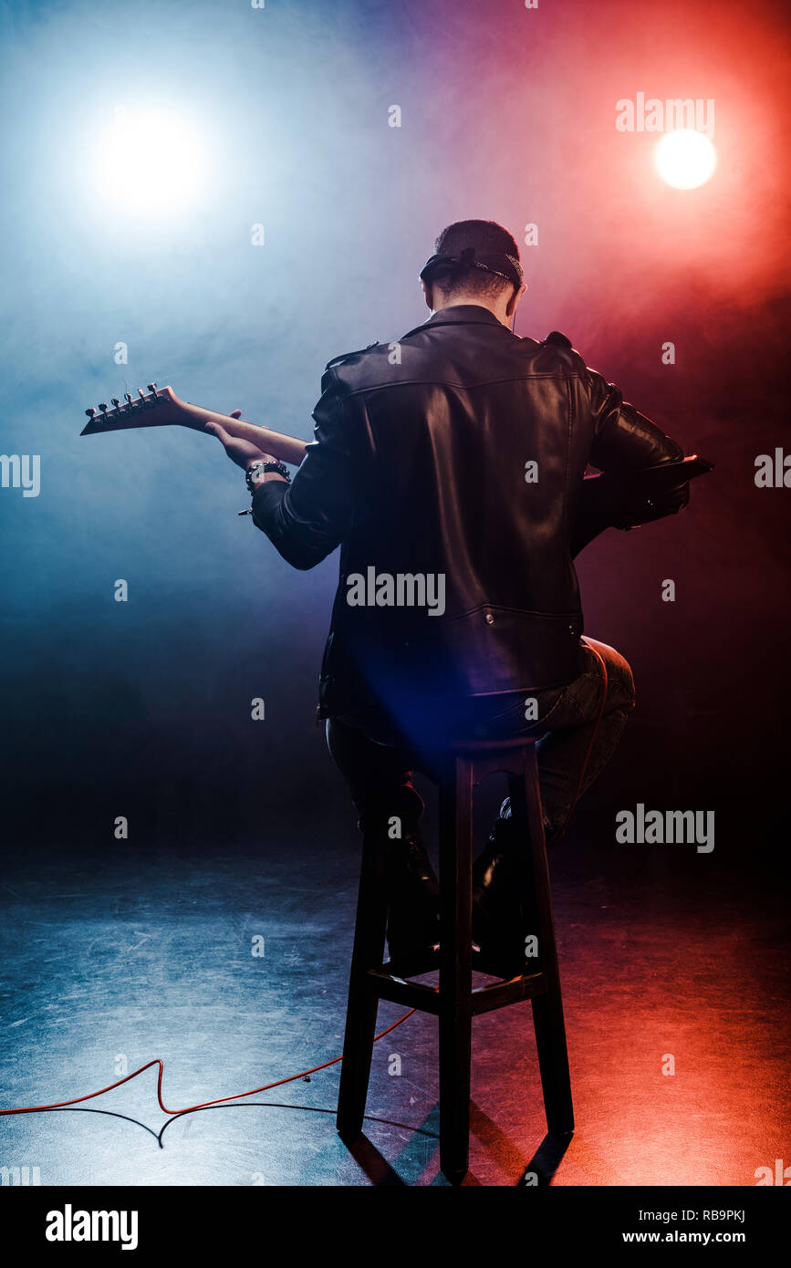 rear view of male rocker sitting on chair and playing on electric ...