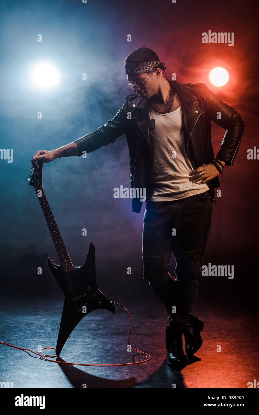 young mixed race rock musician in leather jacket posing with electric ...