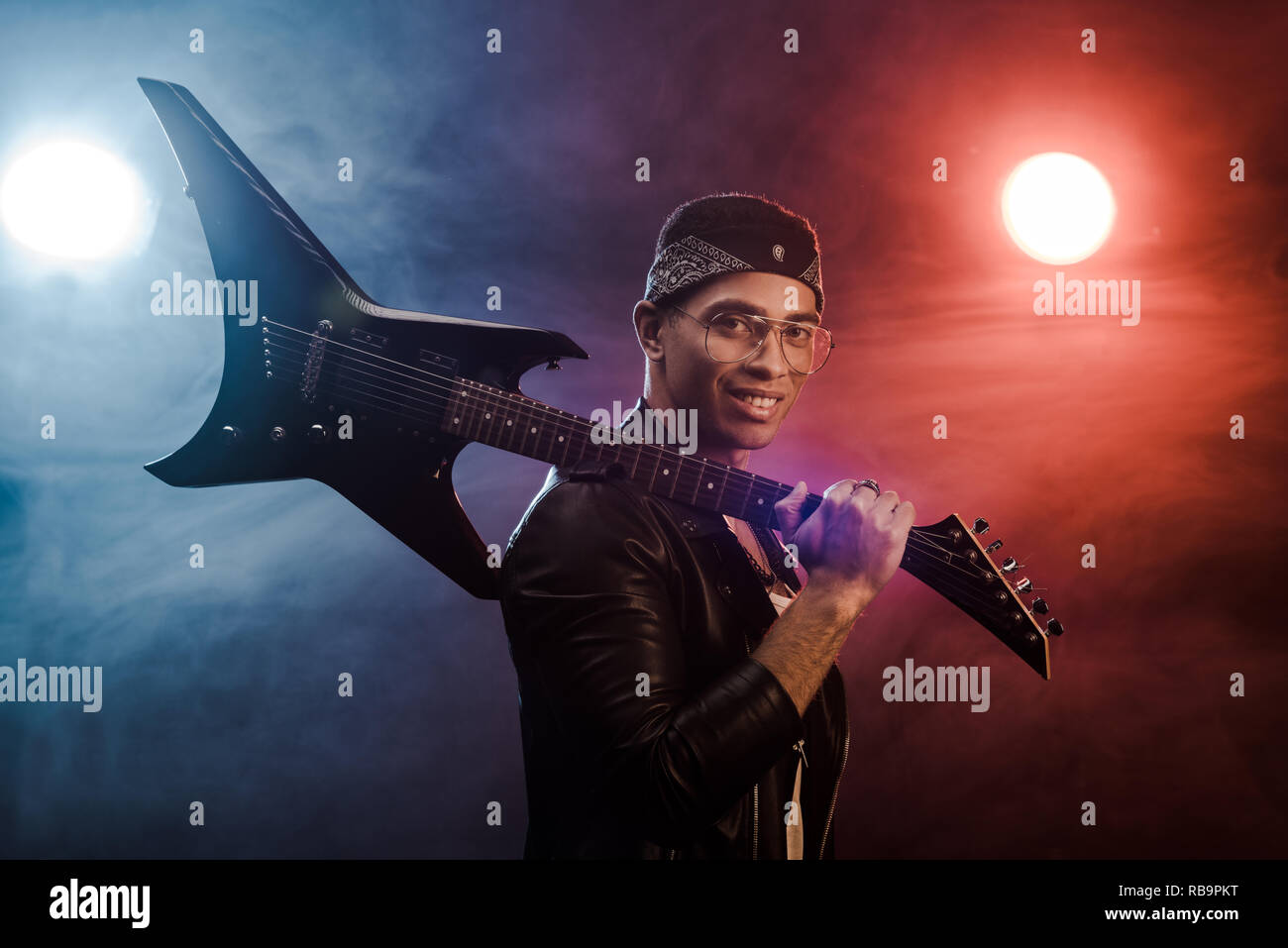 smiling mixed race rock musician in leather jacket posing with electric ...