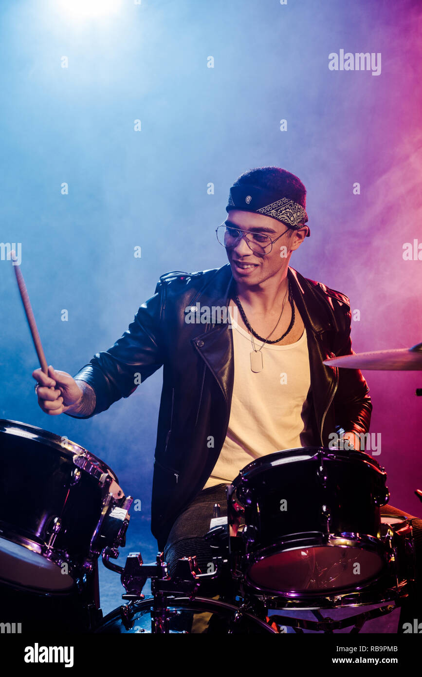 joyful young male musician in leather jacket playing drums during rock ...
