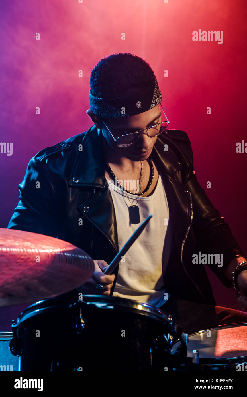 serious young male musician in leather jacket playing drums during rock ...
