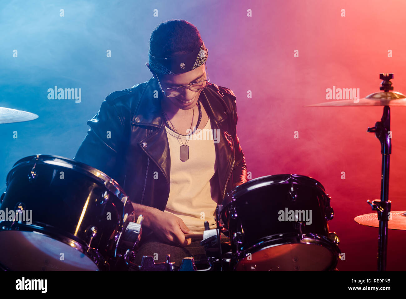 smiling young male musician in leather jacket playing drums during rock ...