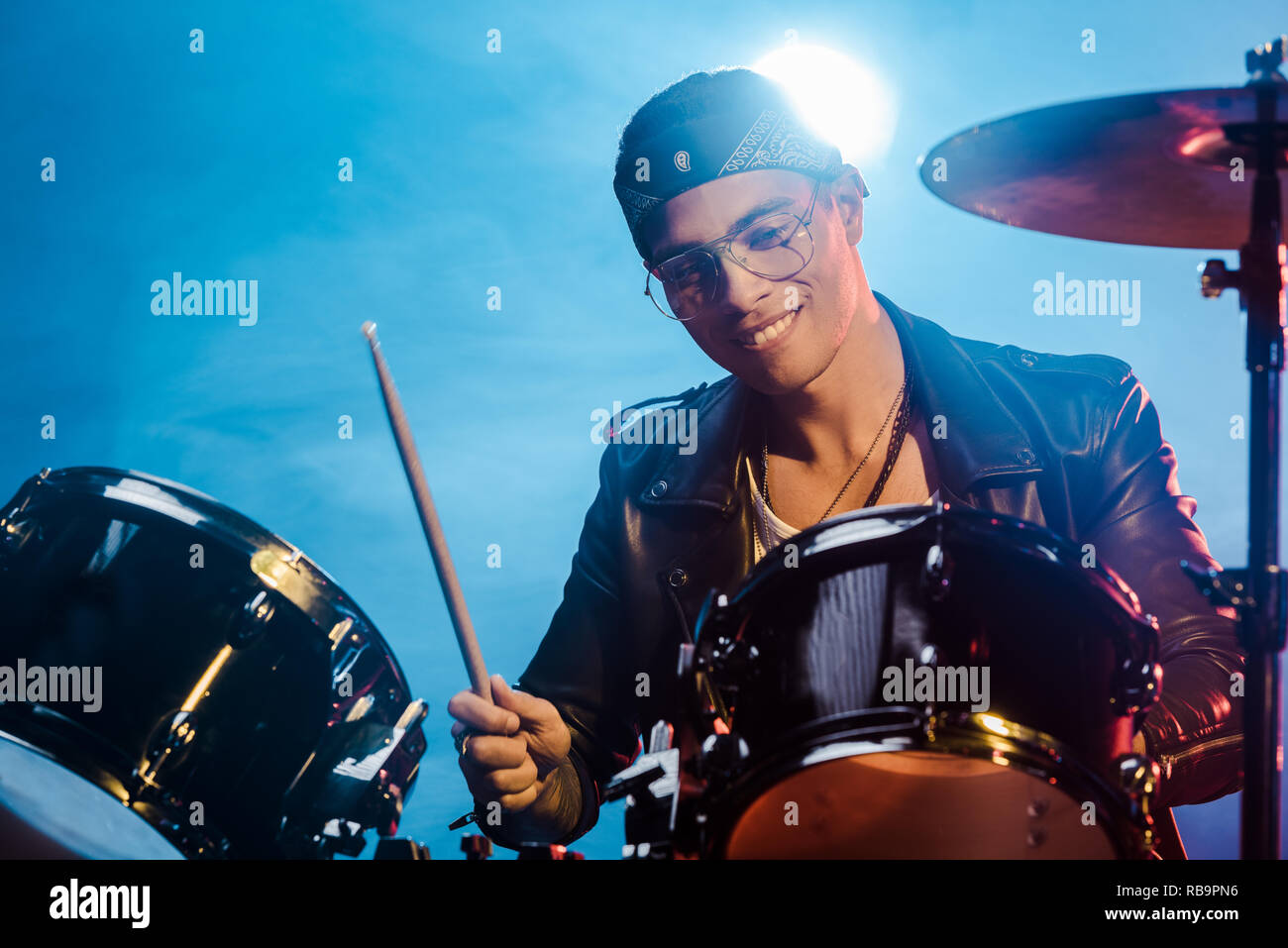 handsome mixed race male musician in leather jacket playing drums ...